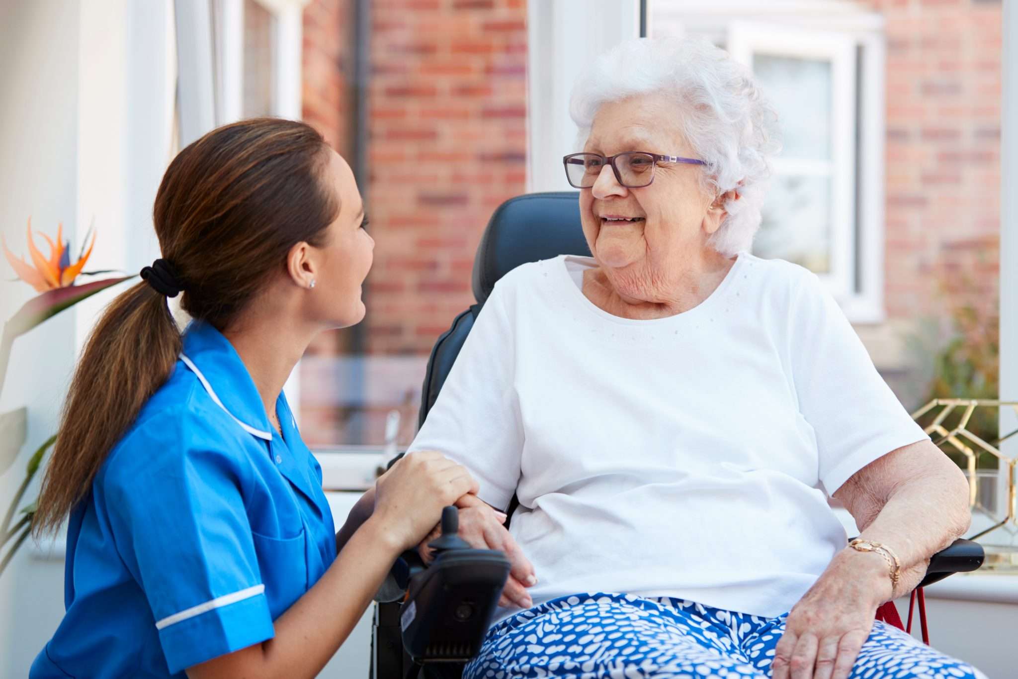 Senior Woman Sitting In Motorized Wheelchair Talking With Nurse In ...